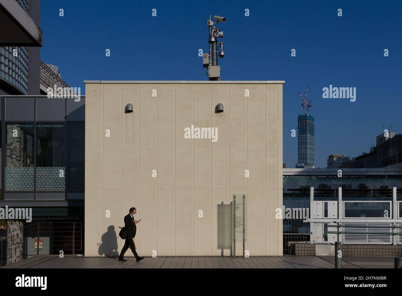 A Japanese office worker or salaryman checks his phone as he walks by a ...