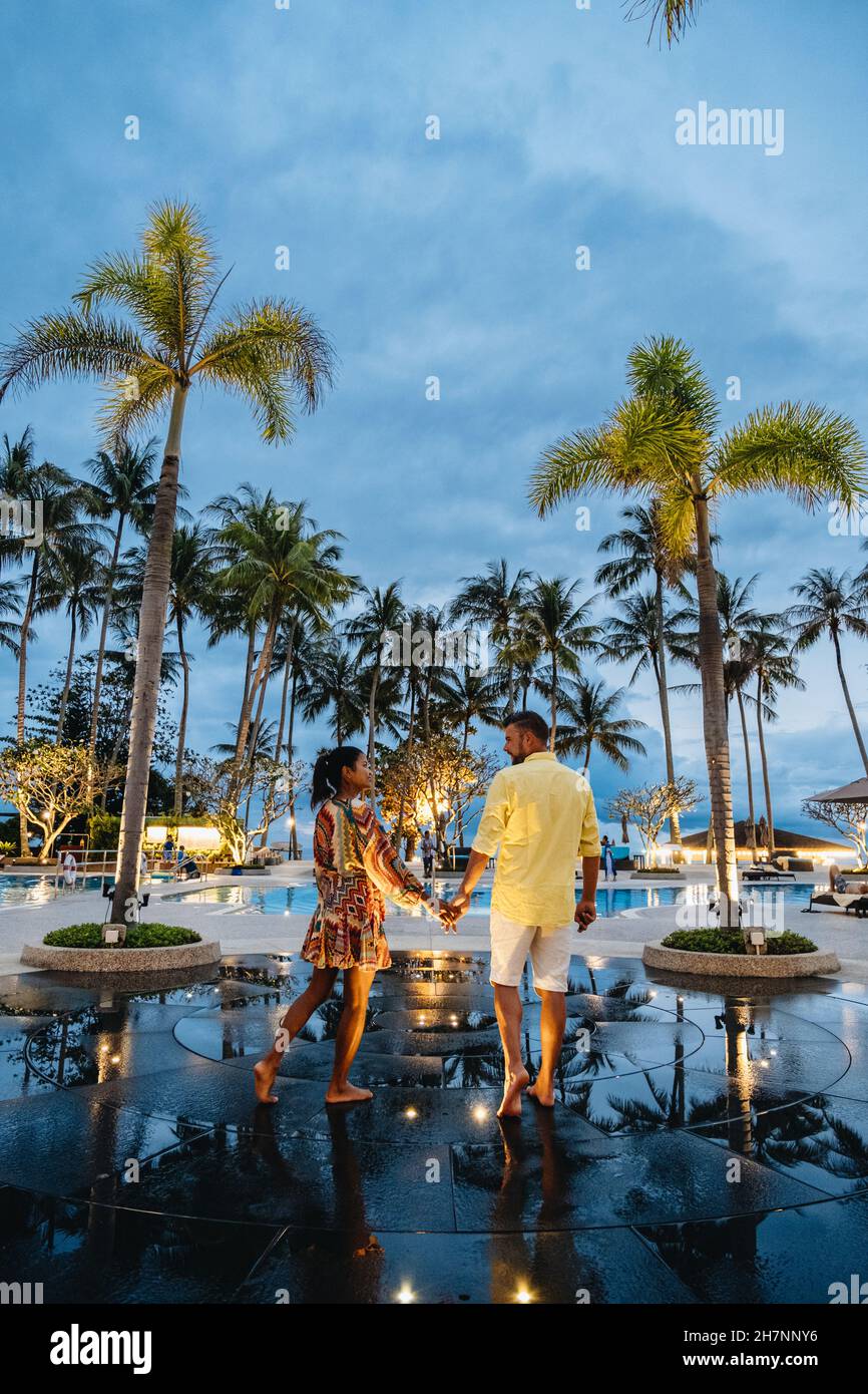 Luxury swimming pool with palm trees at night during sunset in Thailand ...