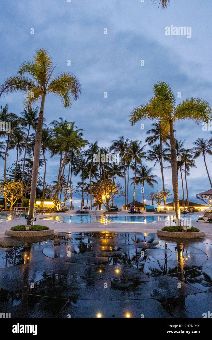 Luxury swimming pool with palm trees at night during sunset in Thailand ...
