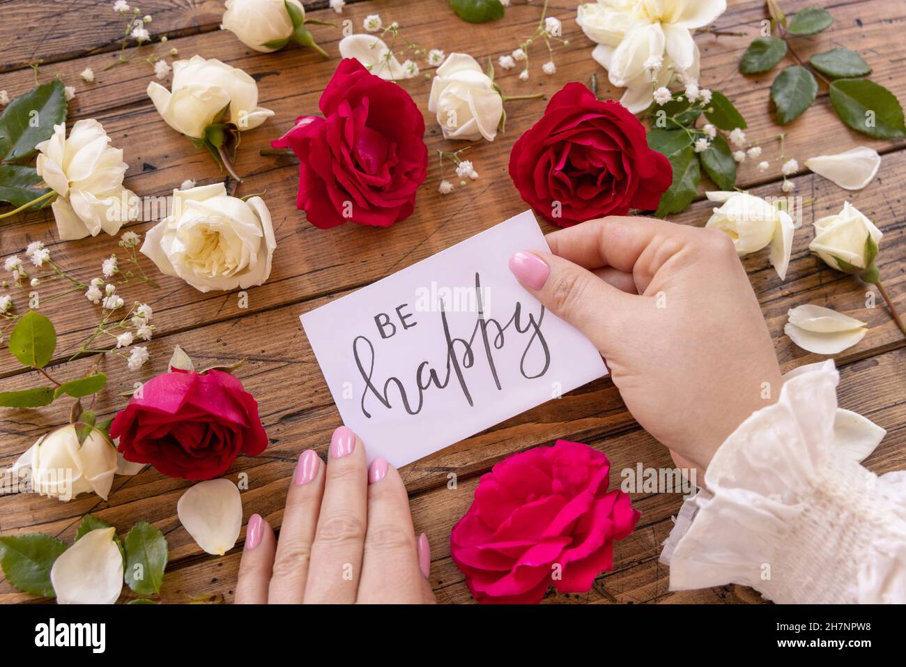 Hands with handwritten card BE HAPPY surrounded by red and cream roses ...