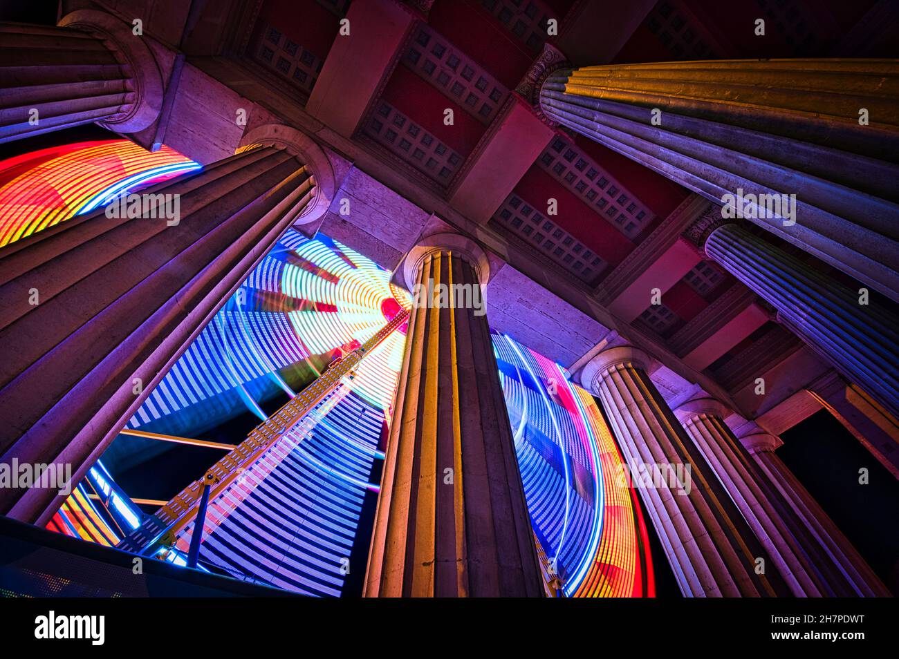Long exposure shot of a giant wheel through greek columns at a funfair ...
