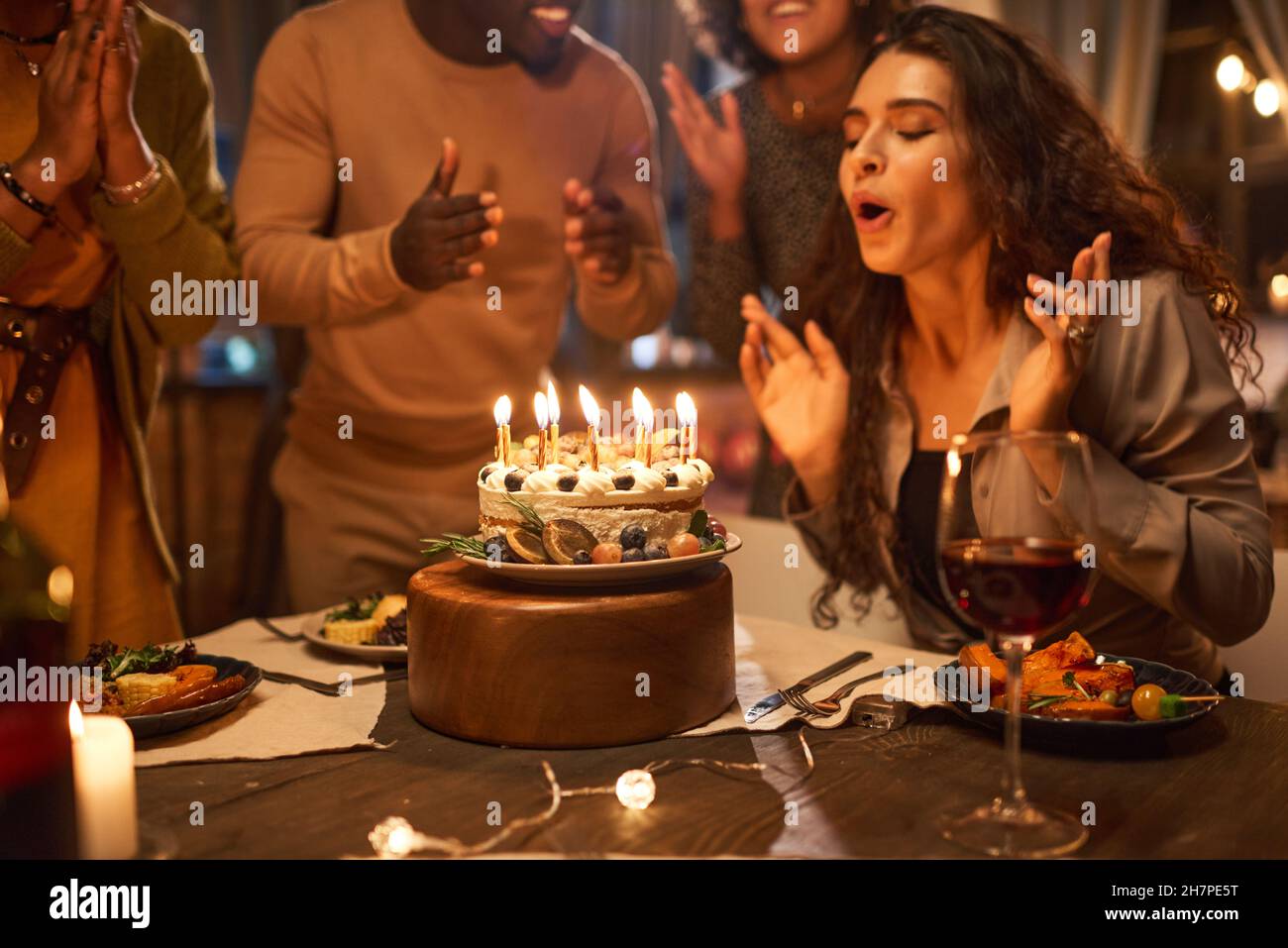 Young woman blowing out candles on birthday cake at the table with her ...