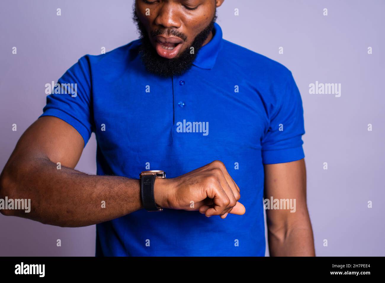 Surprised young African male looking at his watch standing on a pale ...