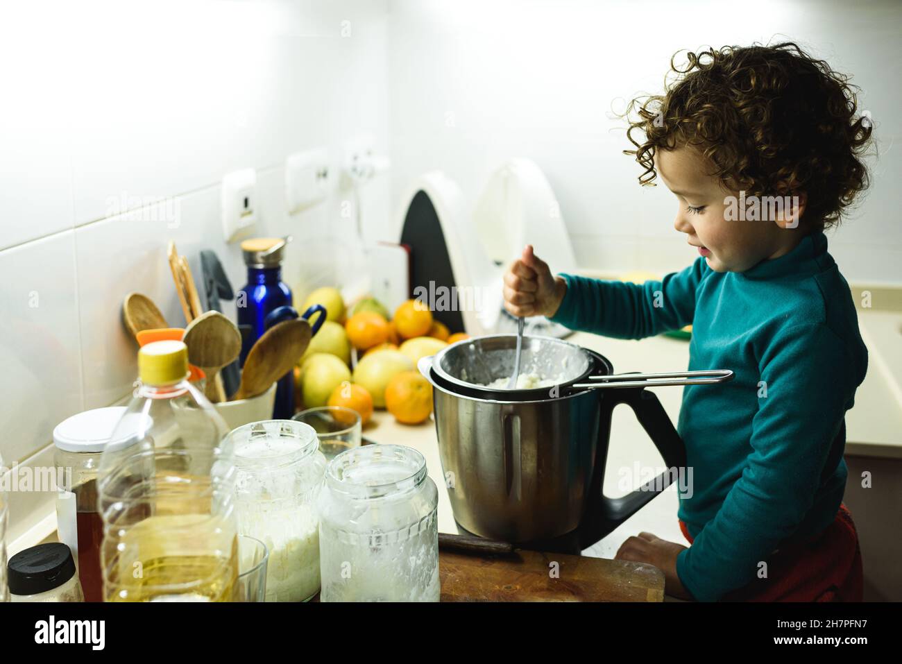 Little curly-haired girl plays cooking in a real kitchen with natural ...