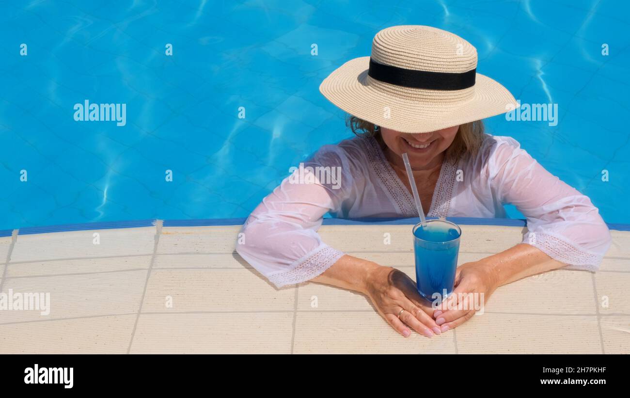 Smiling senior woman relaxing near the blue outdoor swimming pool with ...
