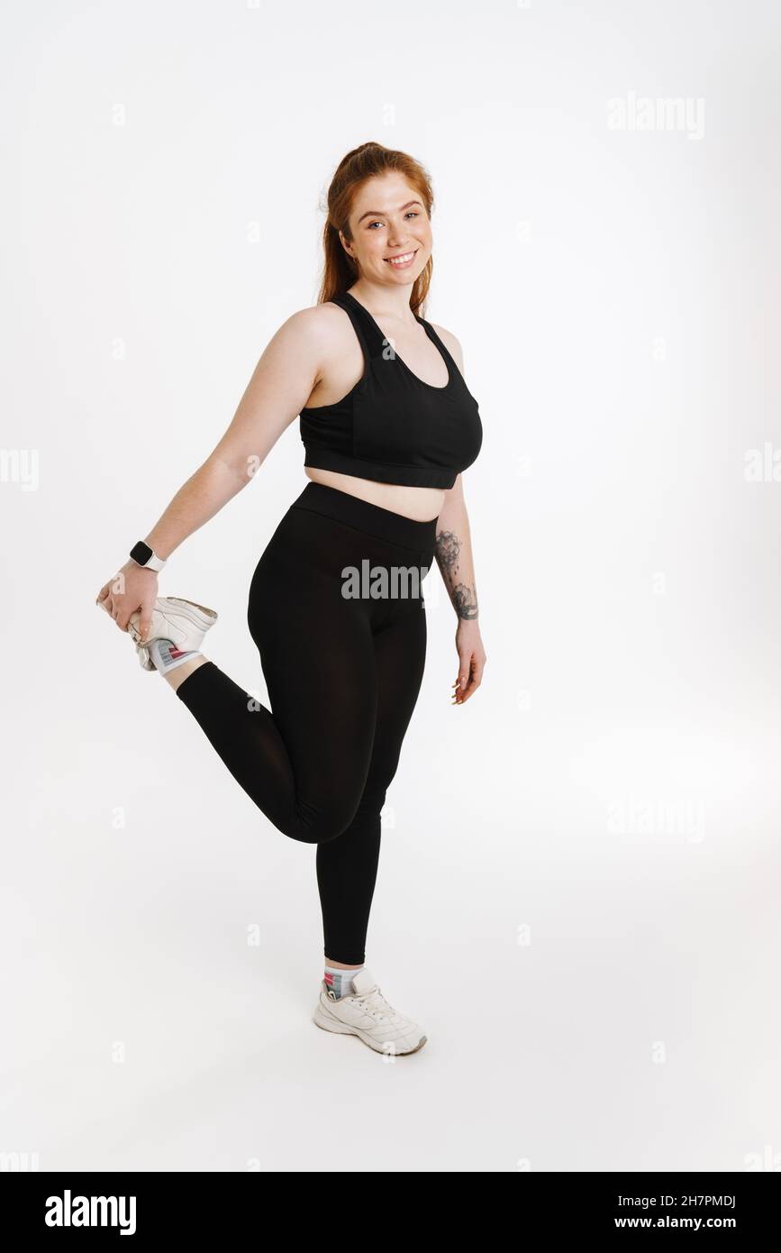 Smiling young plus size fitness woman in sportswear standing over white ...