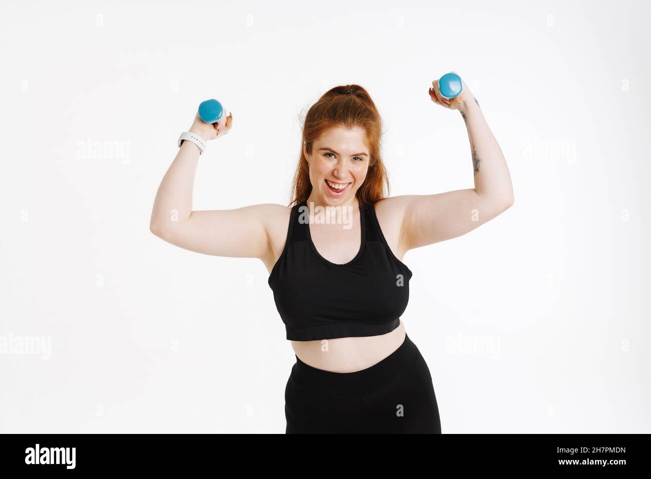 Smiling young plus size fitness woman in sportswear standing over white ...
