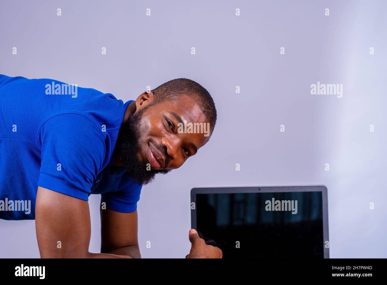 Young African male showing his laptop screen on a pale purple ...
