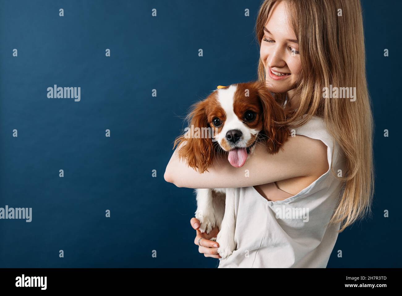 Young smiling pet owner holding her cute little dog in studio against a ...
