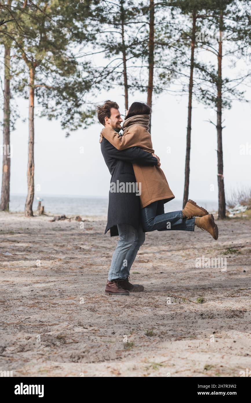 side view of young couple embracing during autumn walk in forest near ...