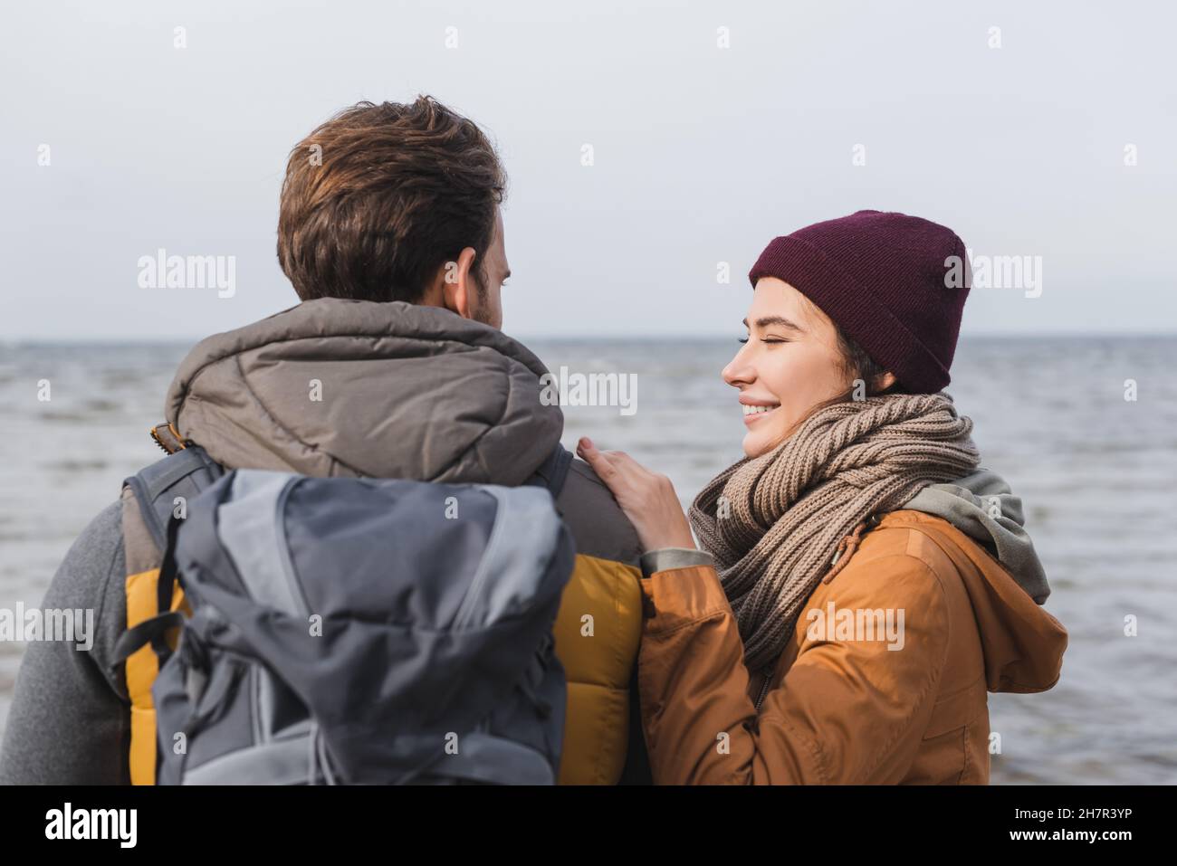 back view of man with backpack near smiling woman touching his shoulder ...