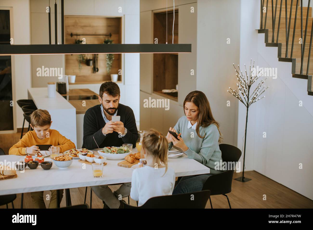 Family using mobile phones while having breakfast at dining table at ...