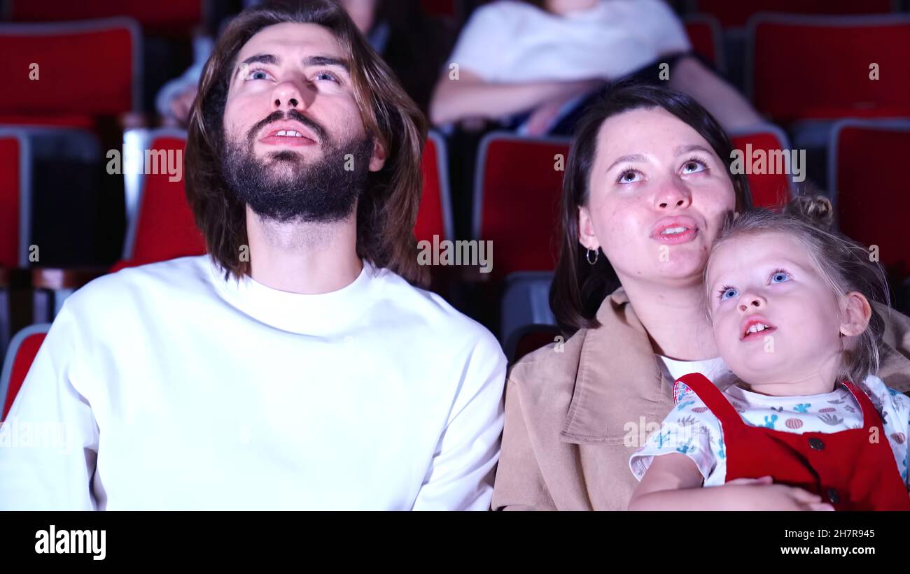 Friendly family watching a movie in the cinema. Young parents and their ...