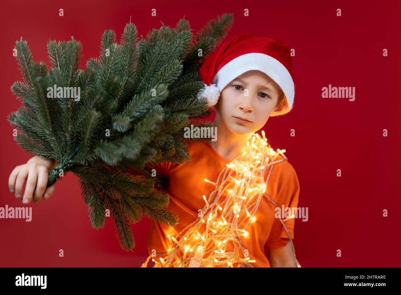 a boy in a red Santa hat and a Christmas garland around his neck is ...