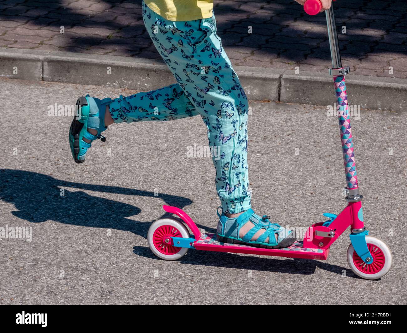 Young anonymous elementary age child riding a simple colorful scooter ...