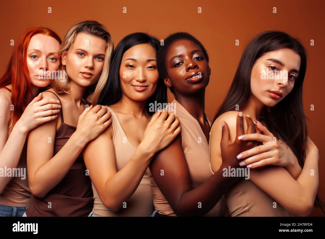 young pretty african and caucasian women posing cheerful together on brown background, lifestyle ...