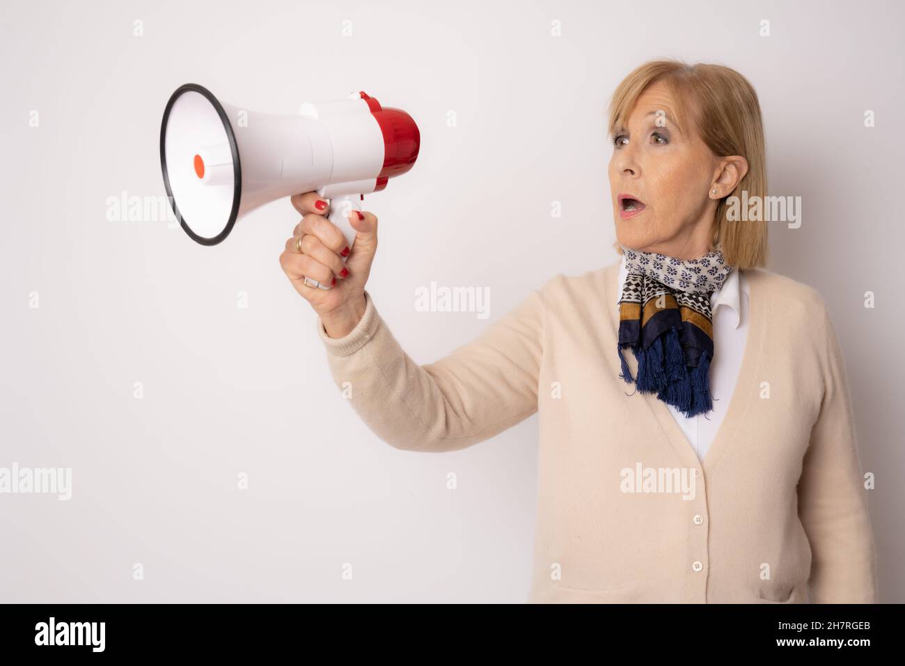 portrait of a happy senior woman shouting with megaphone over white ...