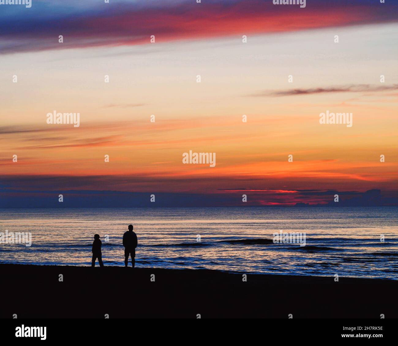 Mesmerizing scene of the sea at sunset and two people in the beach ...