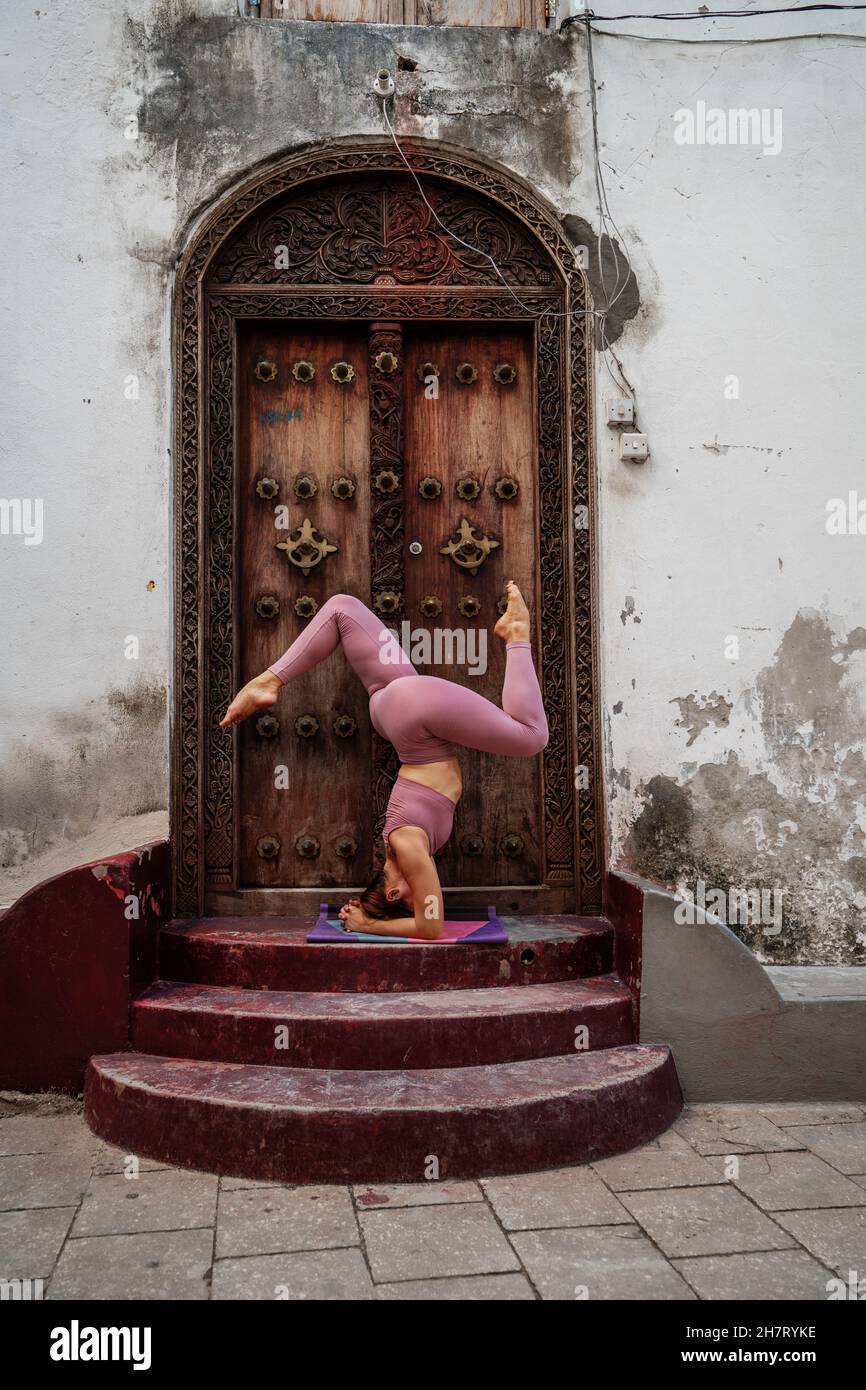Young Caucasian woman doing yoga poses on a mat next to ancient wooden ...