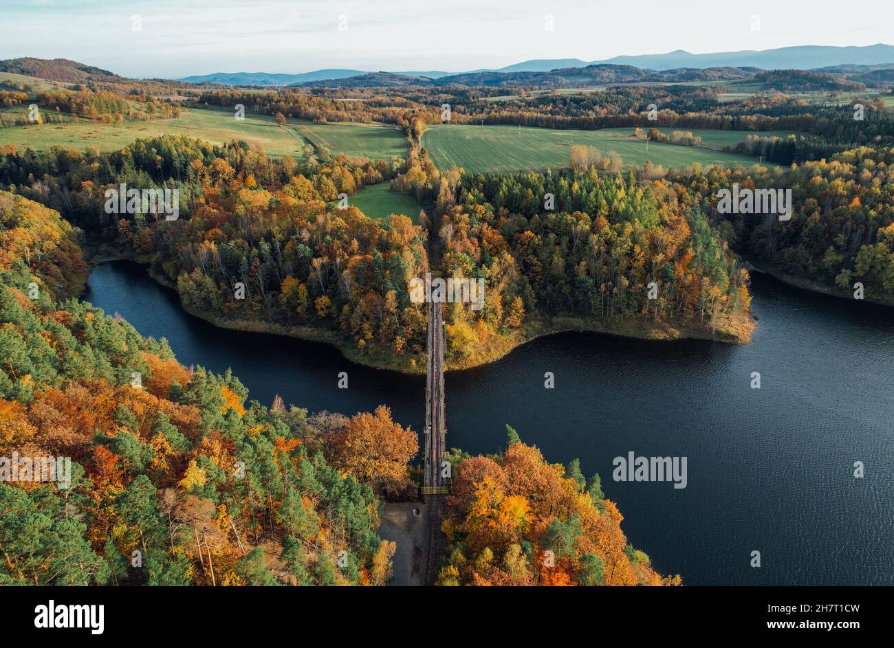 Aerial view of a river with a bridge and fields with colorful trees ...