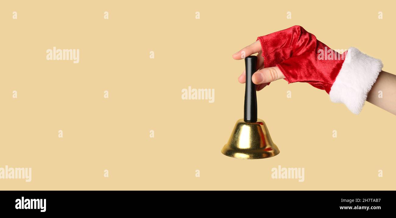 Female hand in mitten holding golden Christmas bell on color background ...
