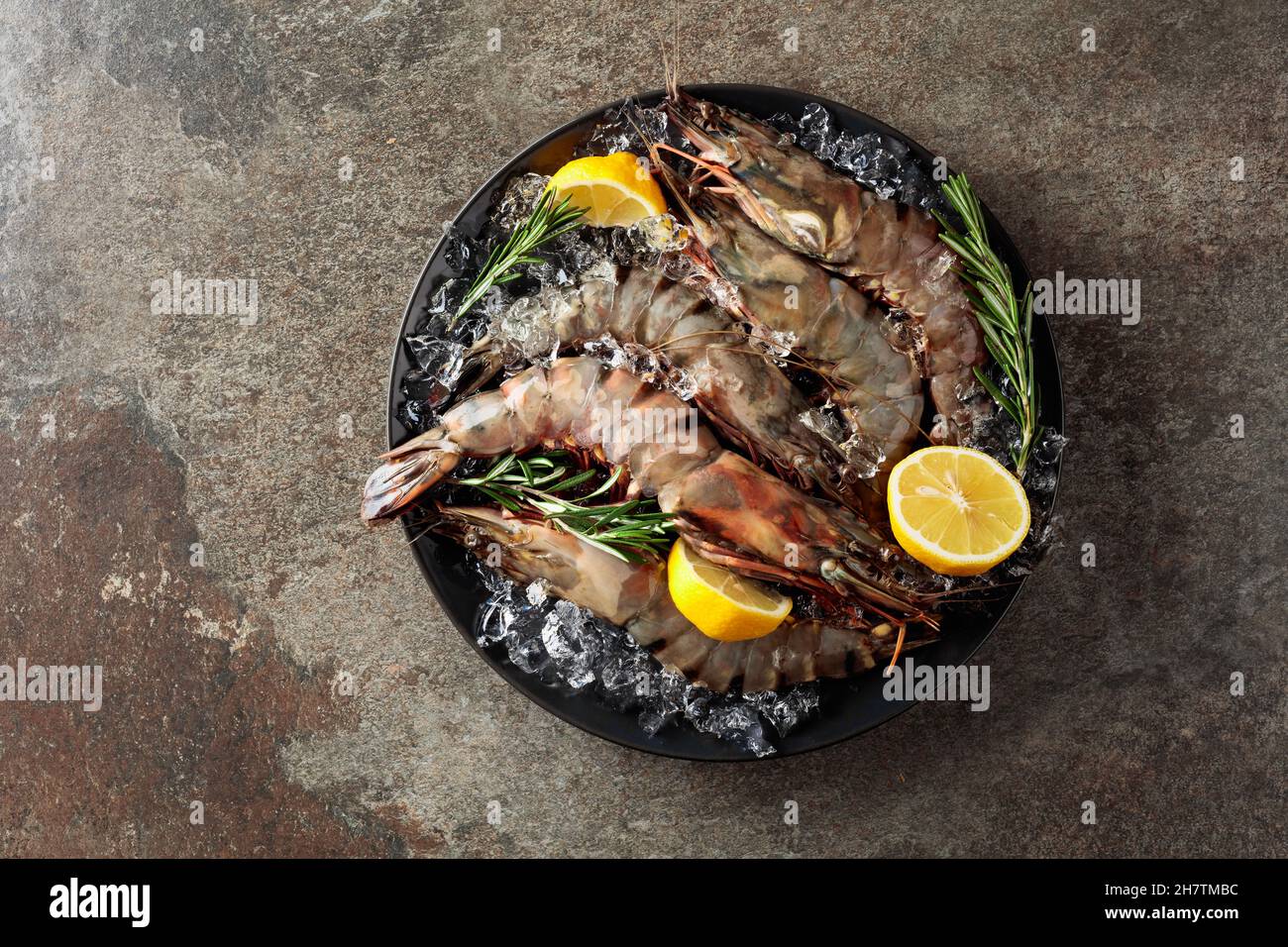 Fresh tiger prawns in a black plate with lemon, rosemary and crushed ...