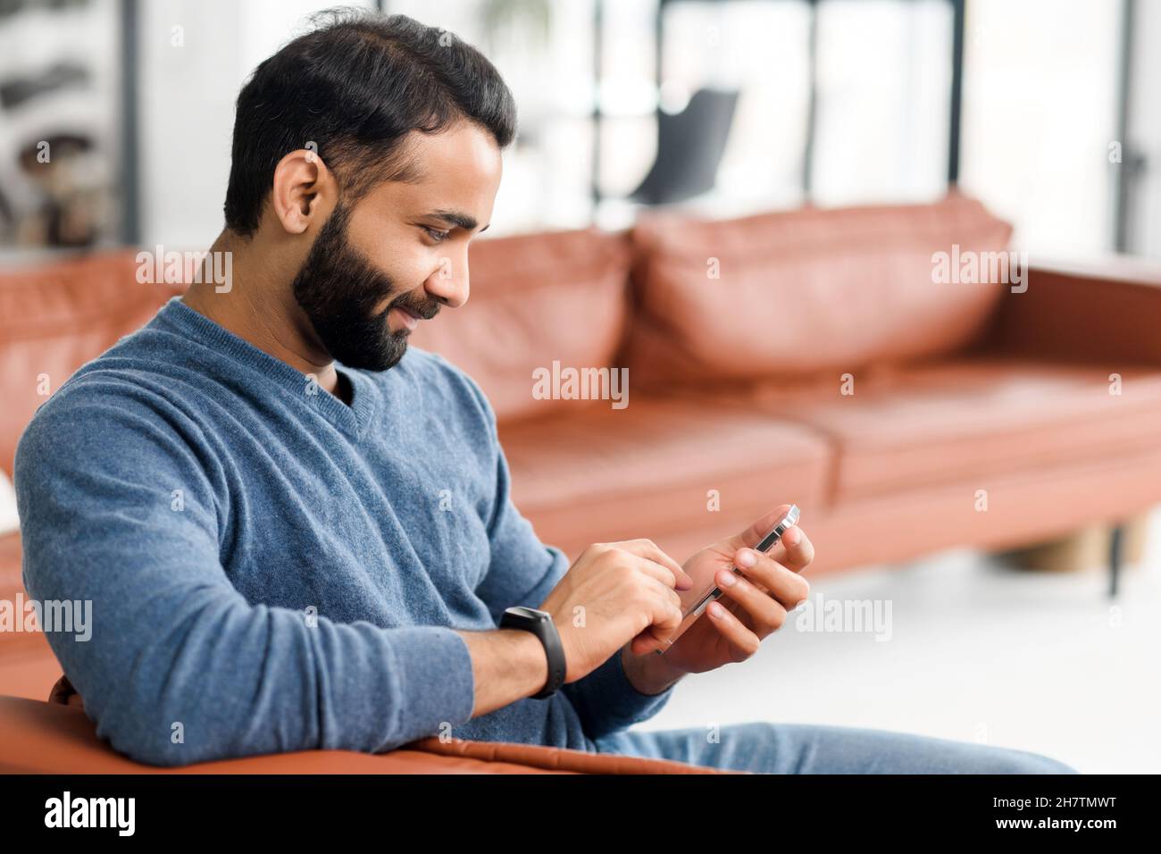 Handsome Indian man sending messages on the smartphone, sitting on the ...