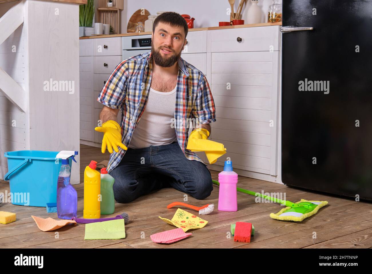 Caucasian young bearded man sits on the floor of his kitchen and tries ...