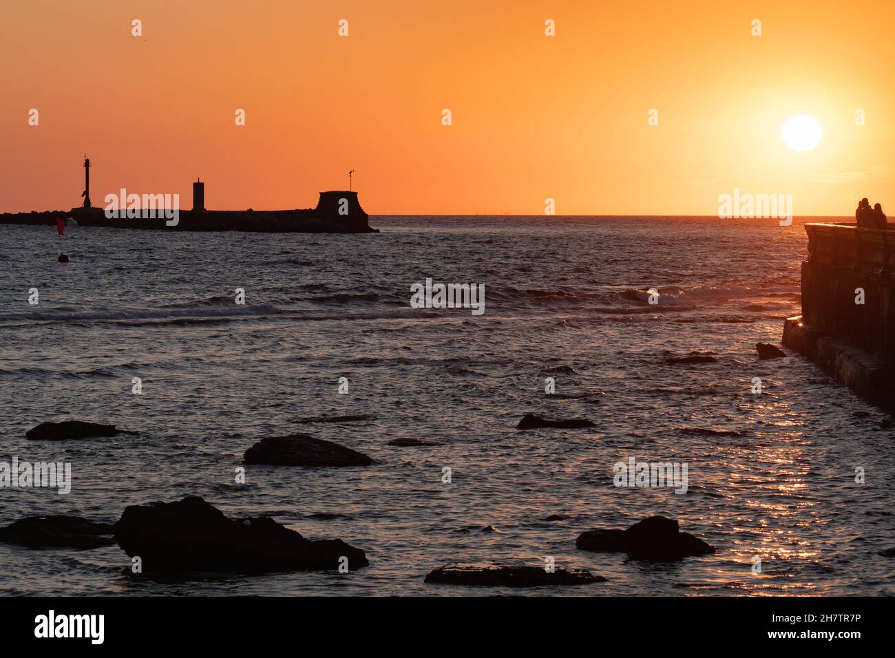Silhouette of Lighthouse, Reef, and Choppy Sea at Sunset Stock Photo ...
