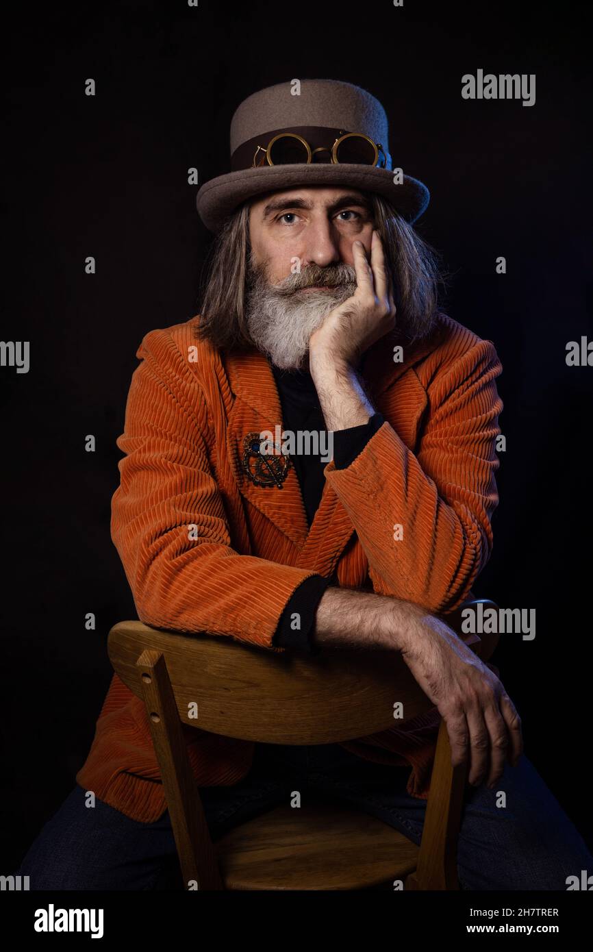 A mature gray-haired bearded intellectual wearing a steampunk hat and ...