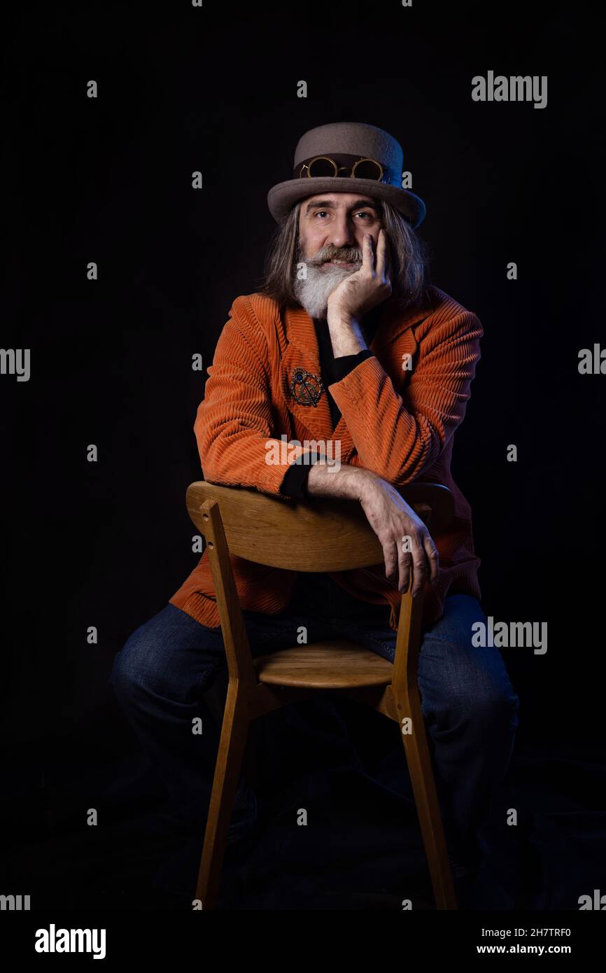 A mature gray-haired bearded intellectual wearing a steampunk hat and ...