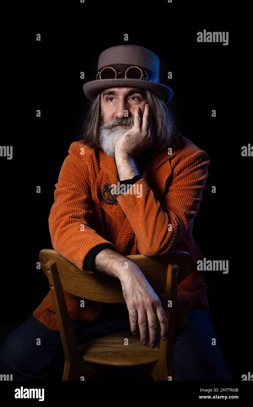 A mature gray-haired bearded intellectual wearing a steampunk hat and ...