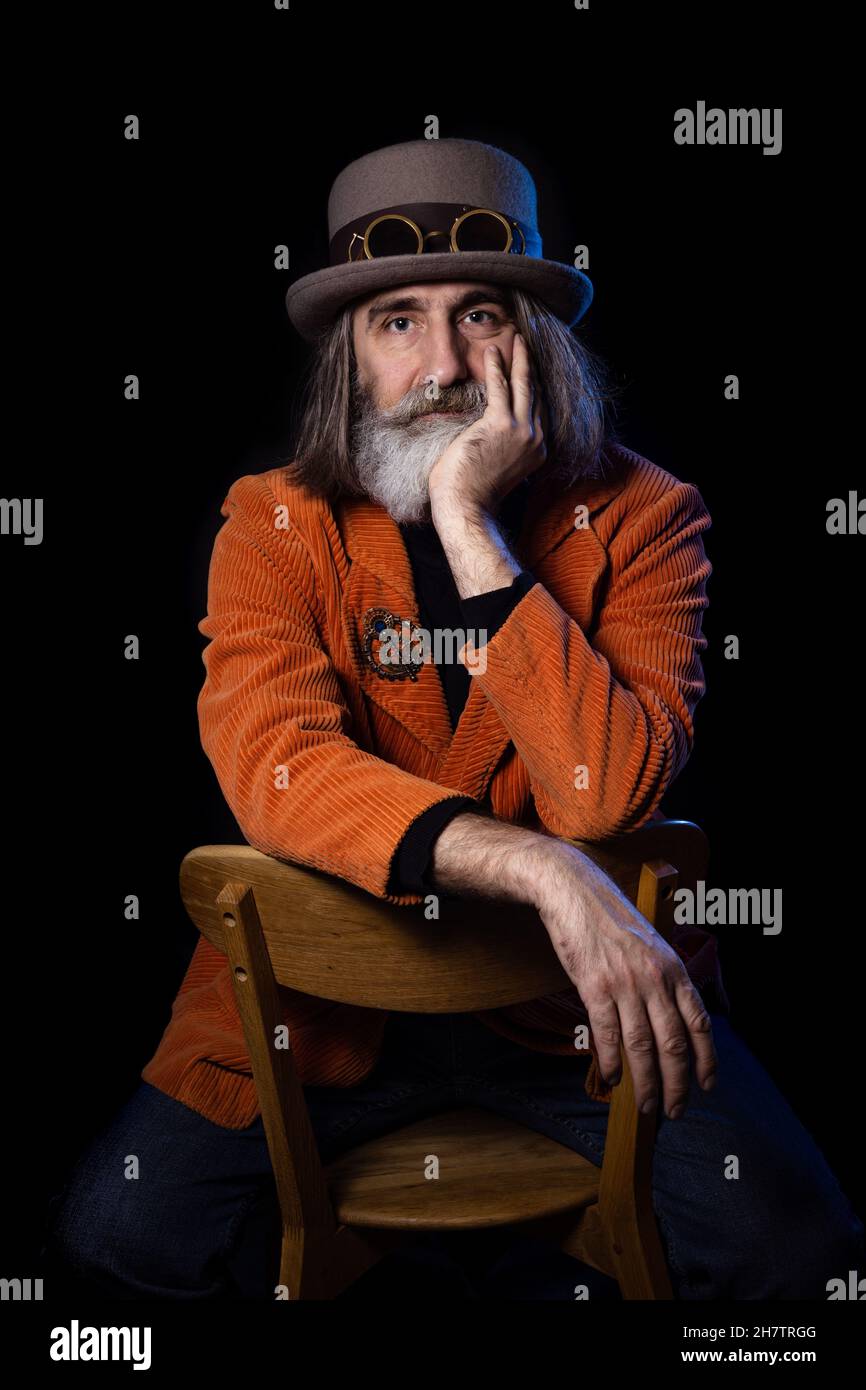 A mature gray-haired bearded intellectual wearing a steampunk hat and ...