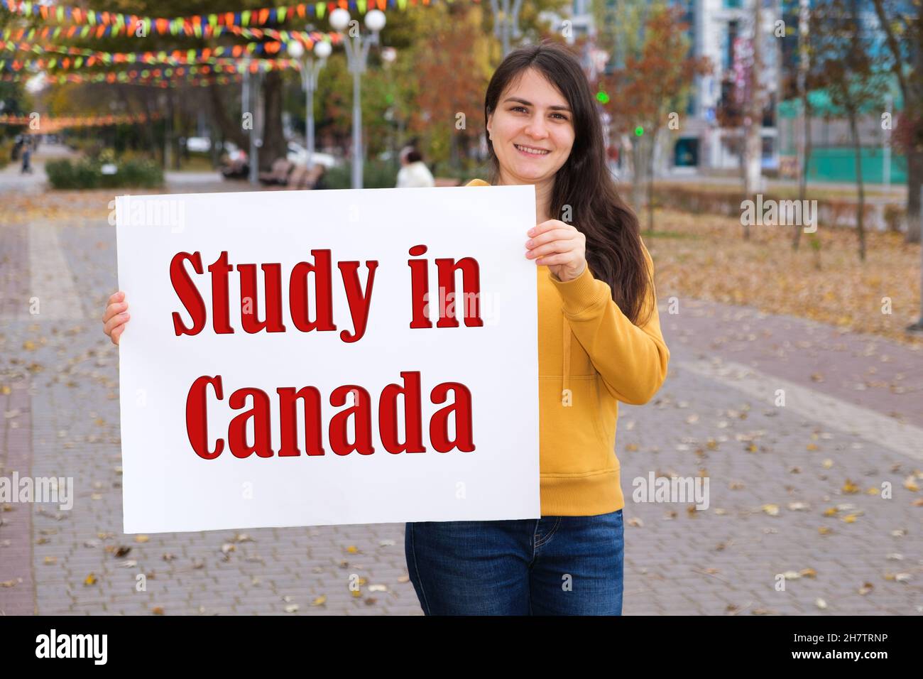 A woman smiles and holds a poster with the text Study in Canada Stock ...