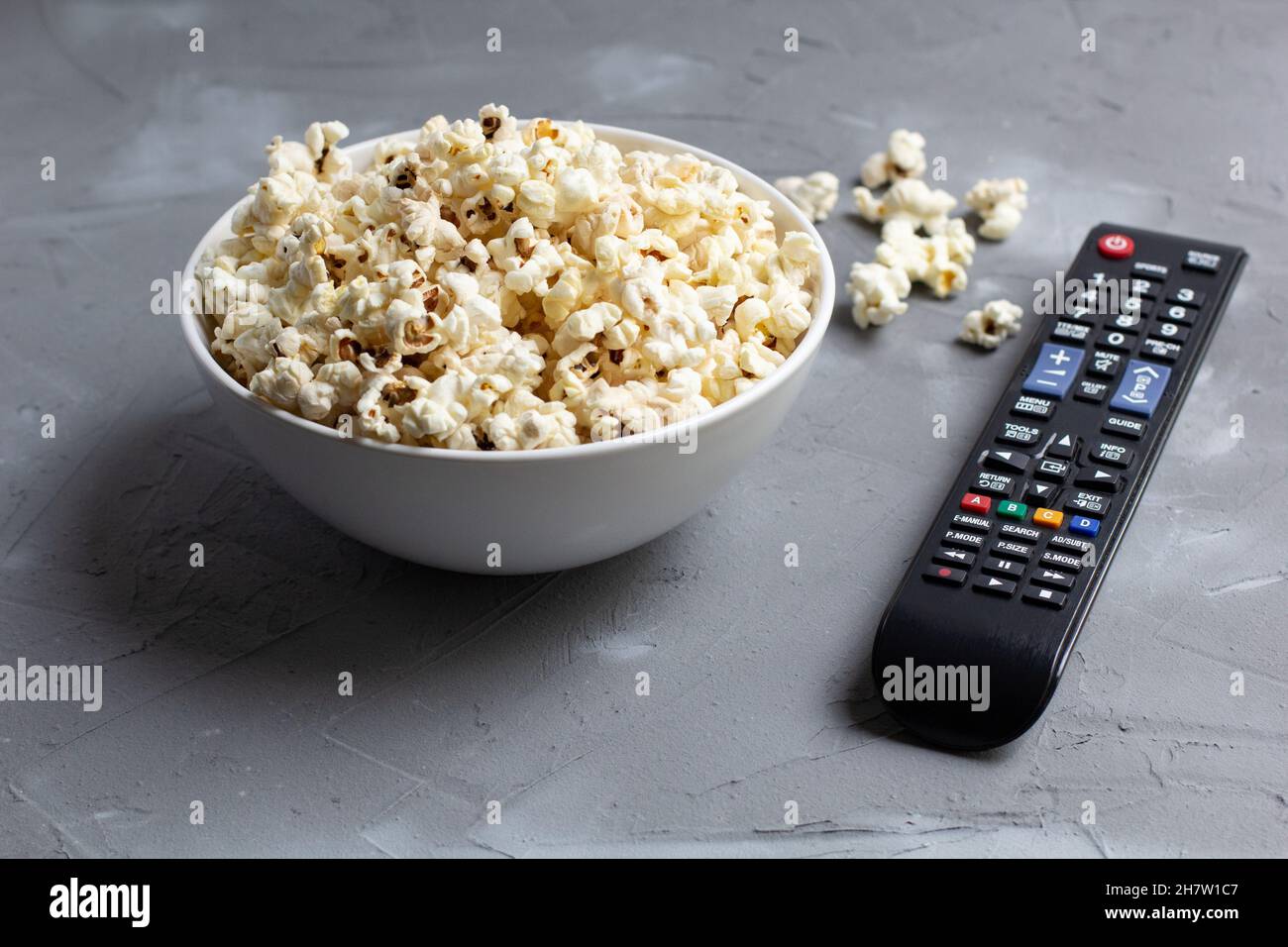 A white bowl of popcorn and TV remote on a grey background. The concept ...