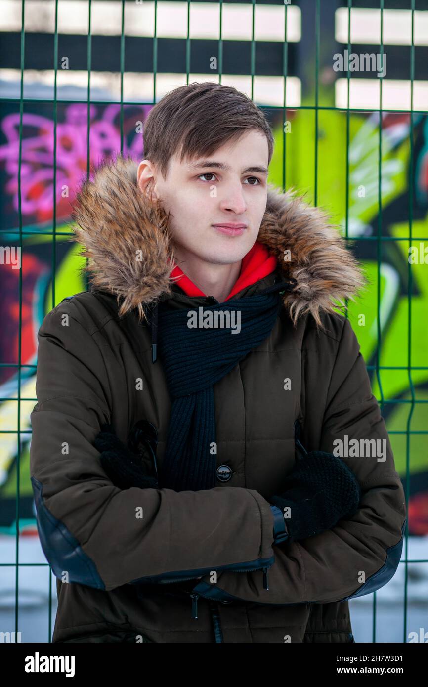 A young man with crossed arms in a winter jacket with fur stands next ...