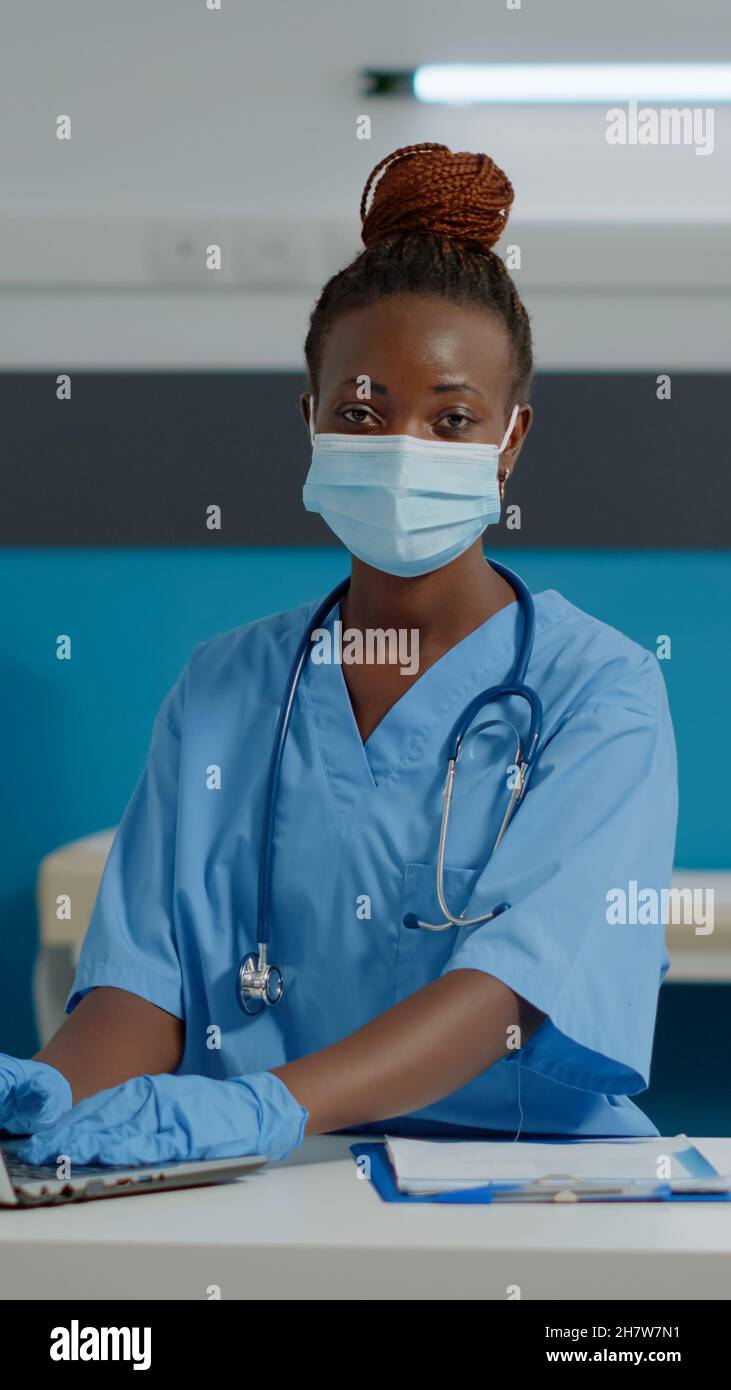 Portrait of medical assistant with uniform and face mask in cabinet at ...