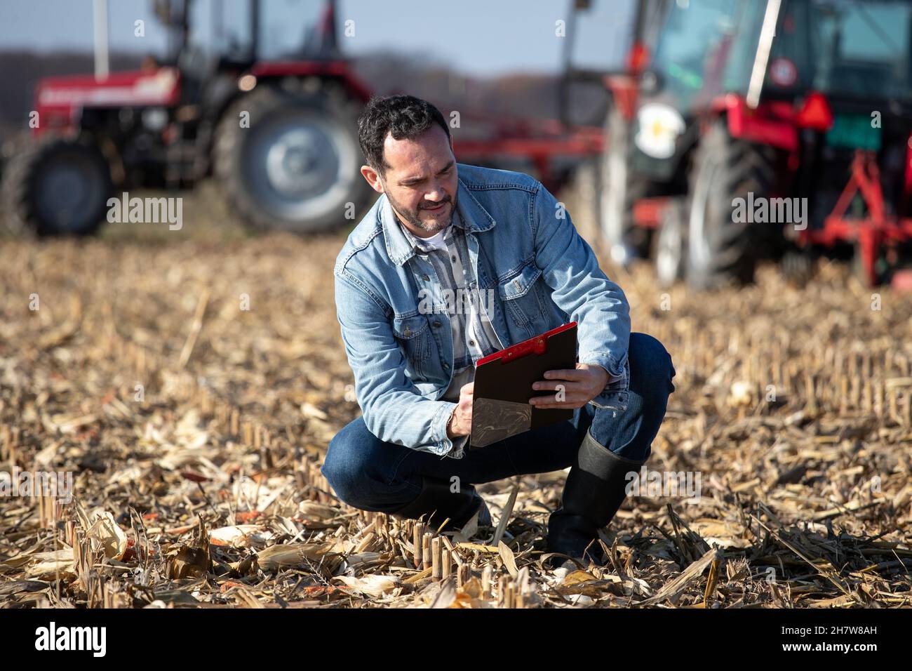 Mature adult farmer squatting in field, writing notes on notepad while ...