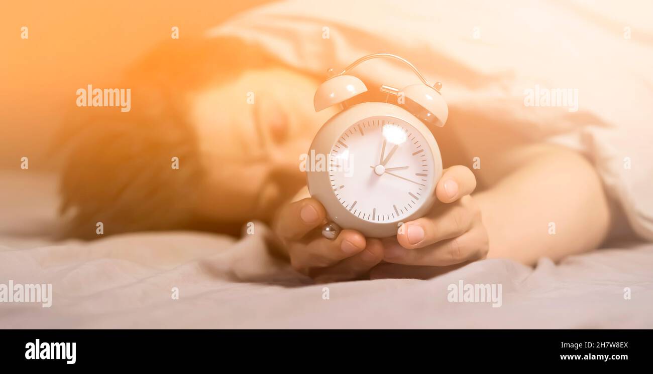 Hands of a young man from under the blankets hold an alarm clock in ...