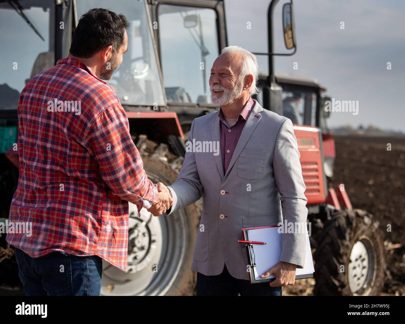 Senior sales representative and mature farmer shaking hands infield in ...