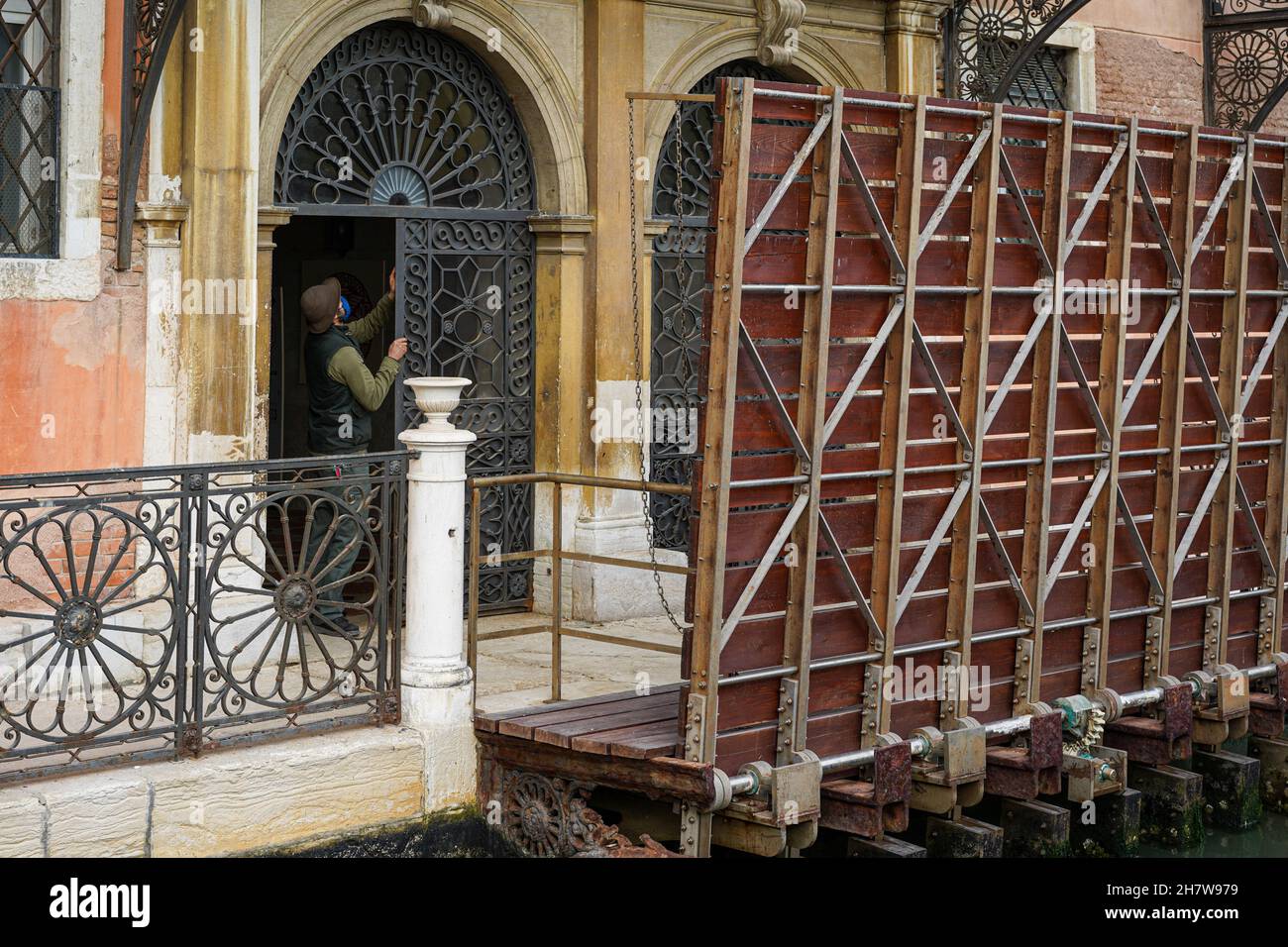 Boat docking on a canal in Venice. Behind a man under a metal entrance ...