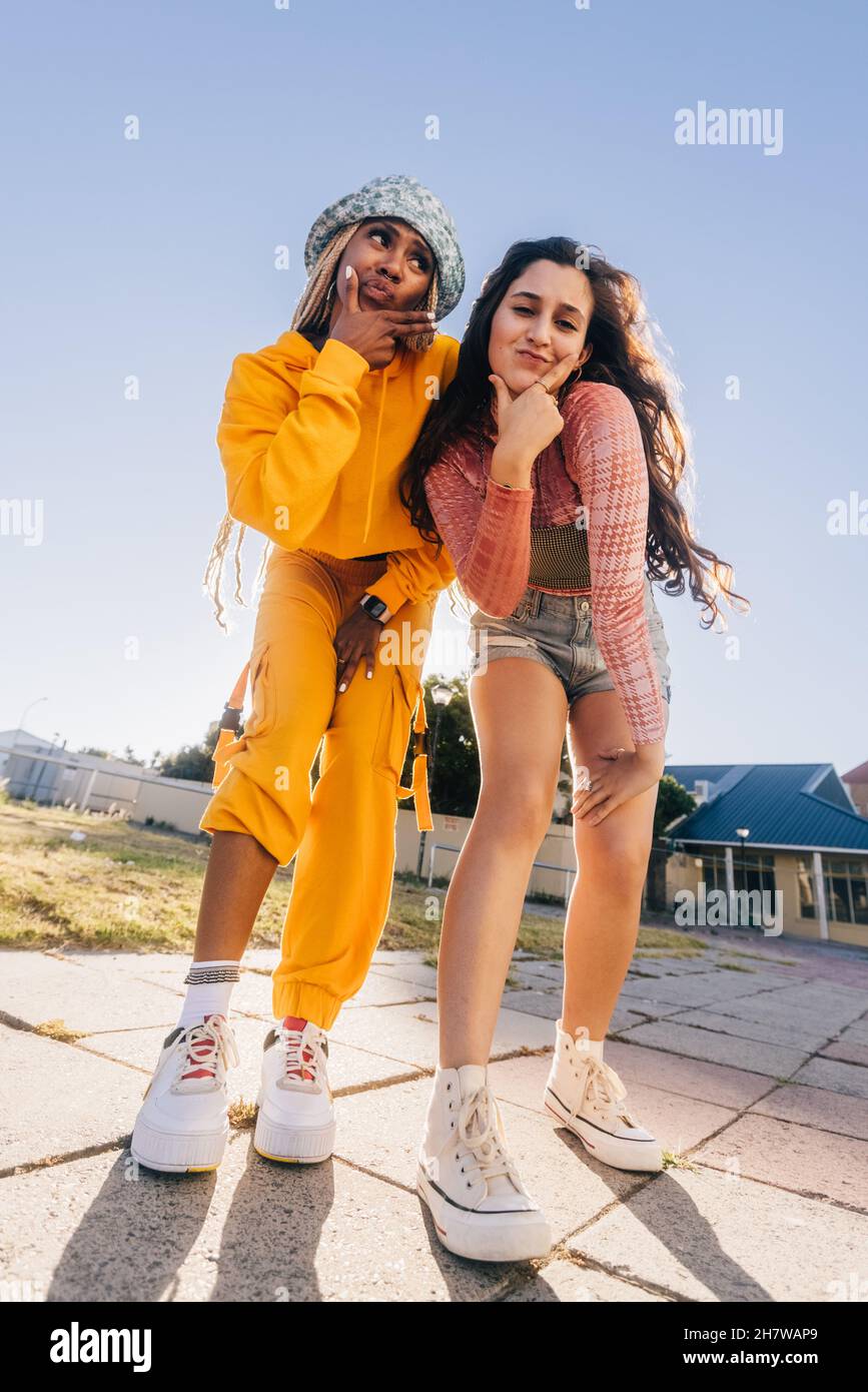 Two female youngsters making gestures while standing together outdoors ...