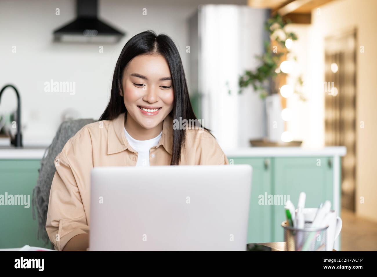 Smiling asian girl using laptop computer, working at home, studying in ...