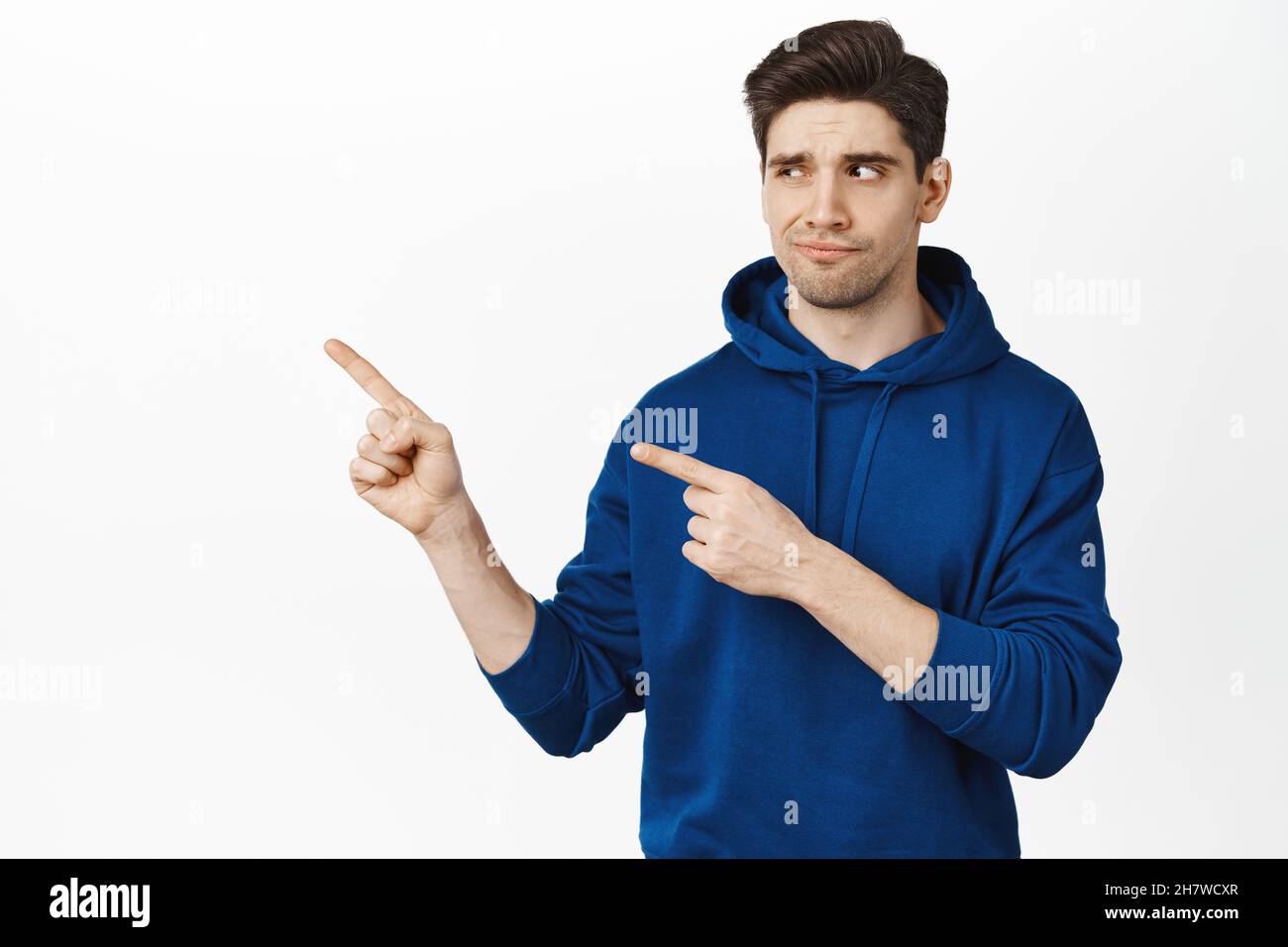 Disappointed brunette guy pointing fingers left, looking upset and ...