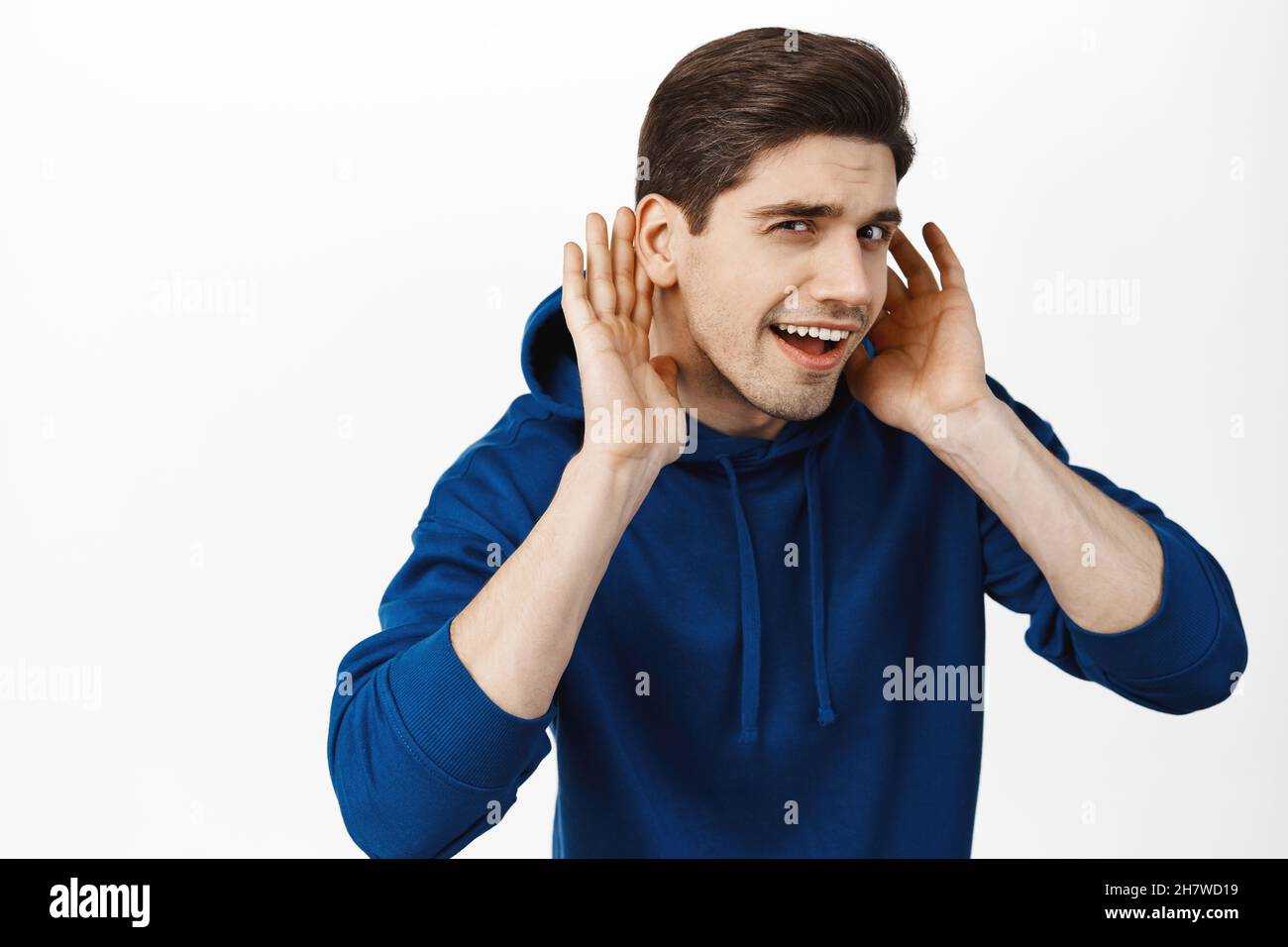 Portrait of eavesdropping guy bending closer and holding hands near ear ...