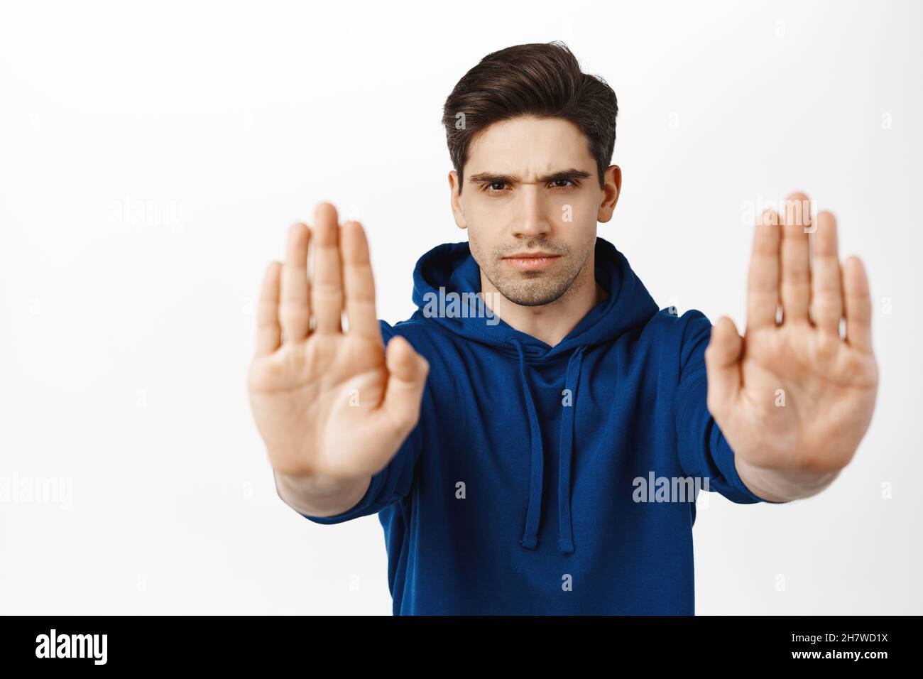 Stop, back off. Serious brunette guy extends palms at camera, telling ...