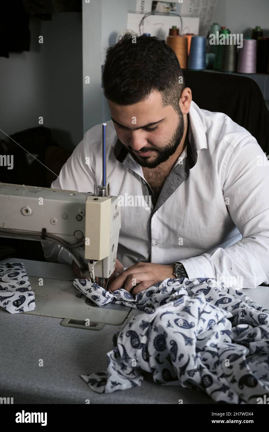 Middle eastern male tailor in white shirt working on sewing machine ...