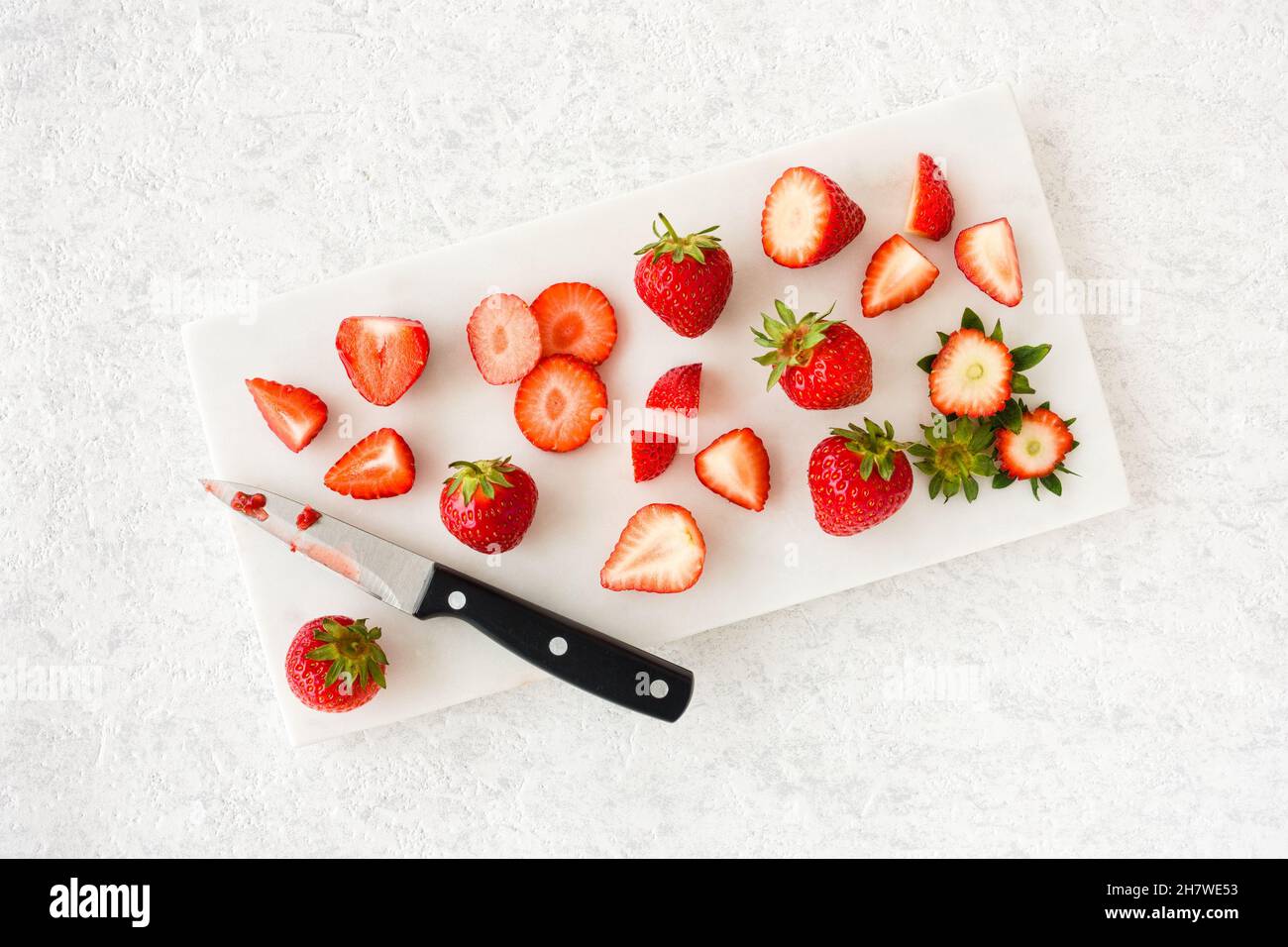 Whole, cut, sliced, quartered and halved strawberries on white marble ...