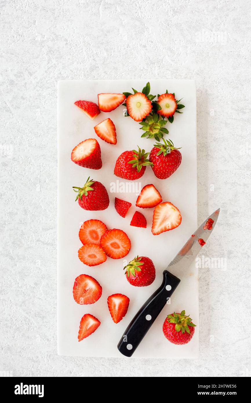 Cut, sliced, quartered, halved and whole strawberries on white marble ...
