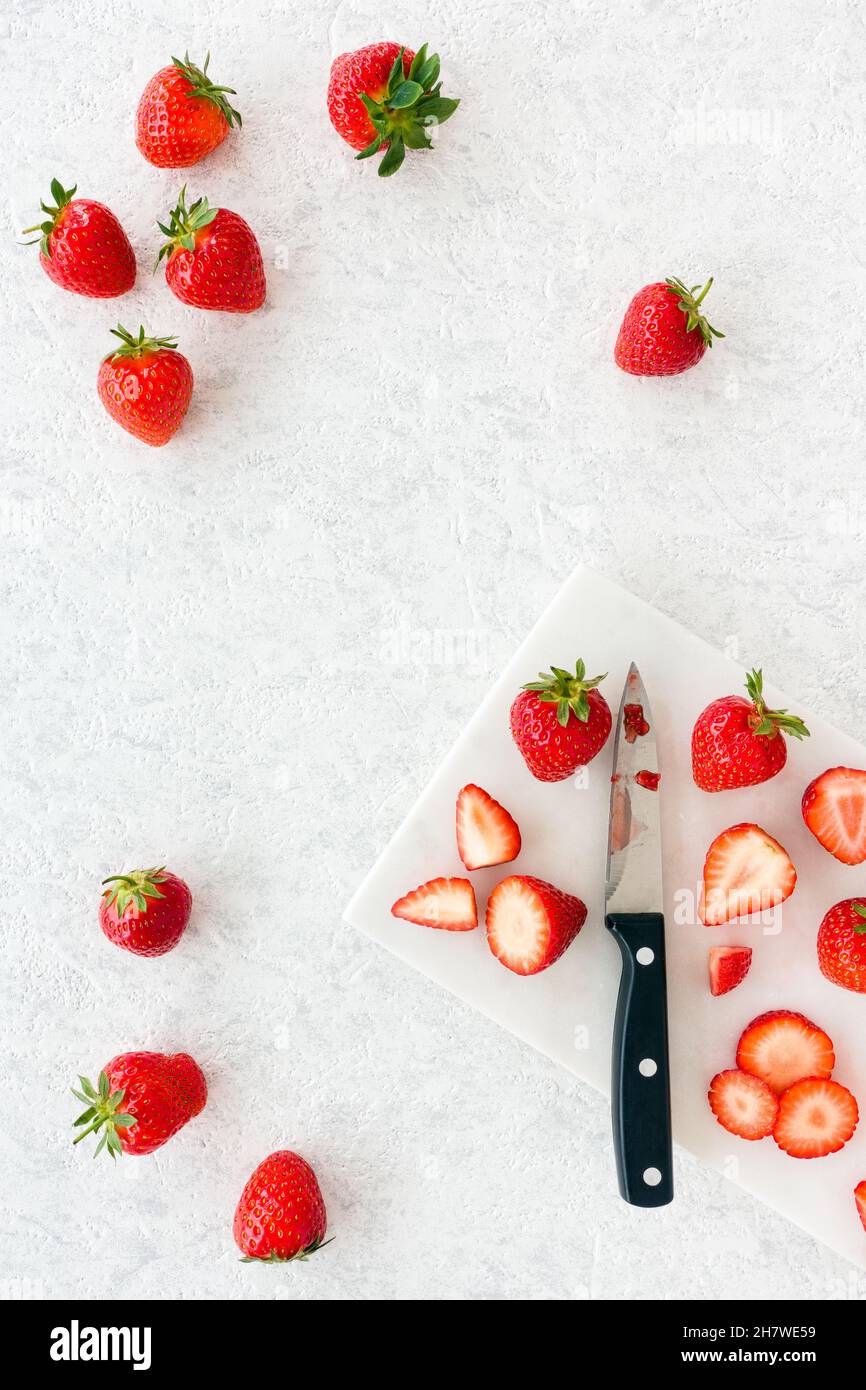 Strawberries, whole and cut, on white marble cutting board with knife ...